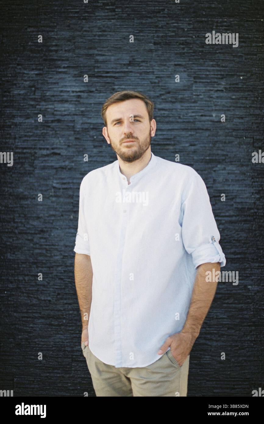 Young Man With His Hands In His Pants Pockets Stands Near A Dark Wall