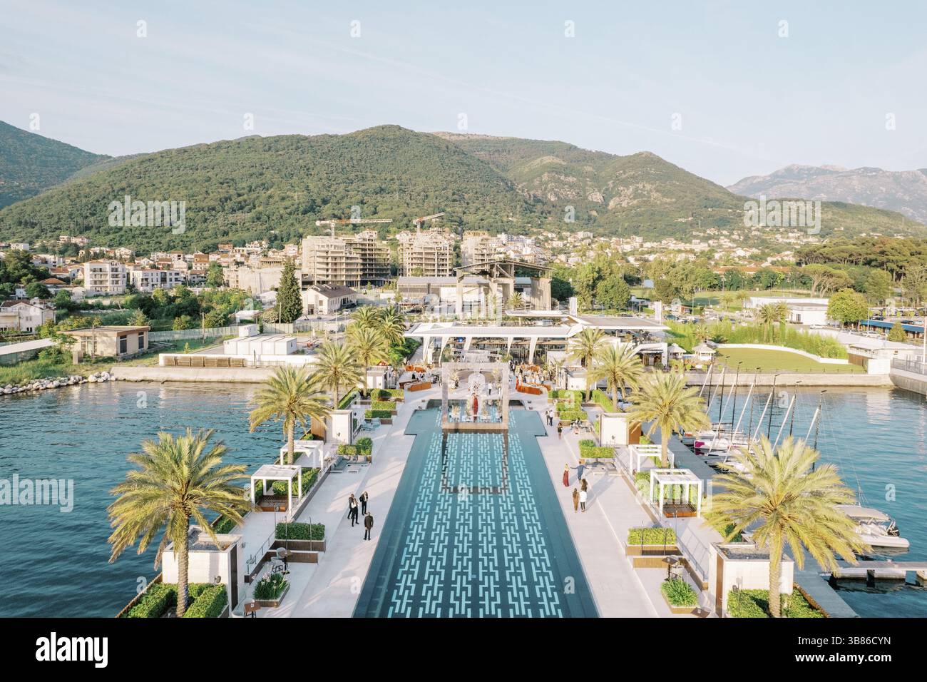 Long swimming pool with green palm trees on a pier near the mountainous ...