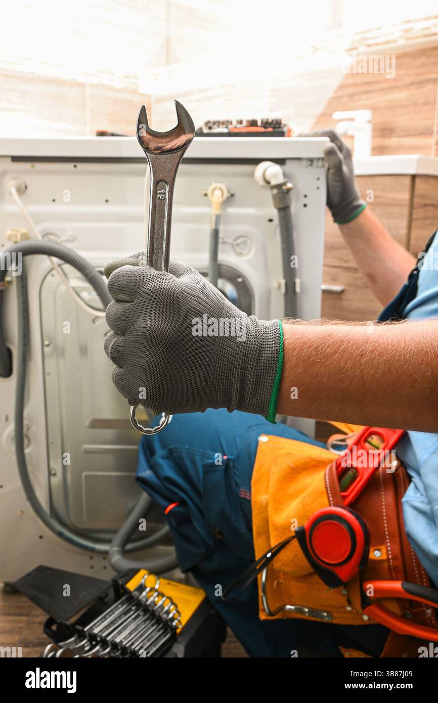 Repairman holding wrench fixing washing machine in bathroom Stock Photo ...
