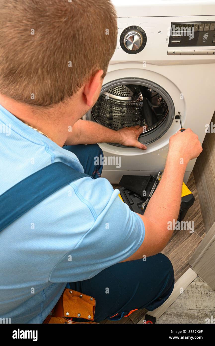 Technician repairing washing machine using screwdriver in bathroom ...