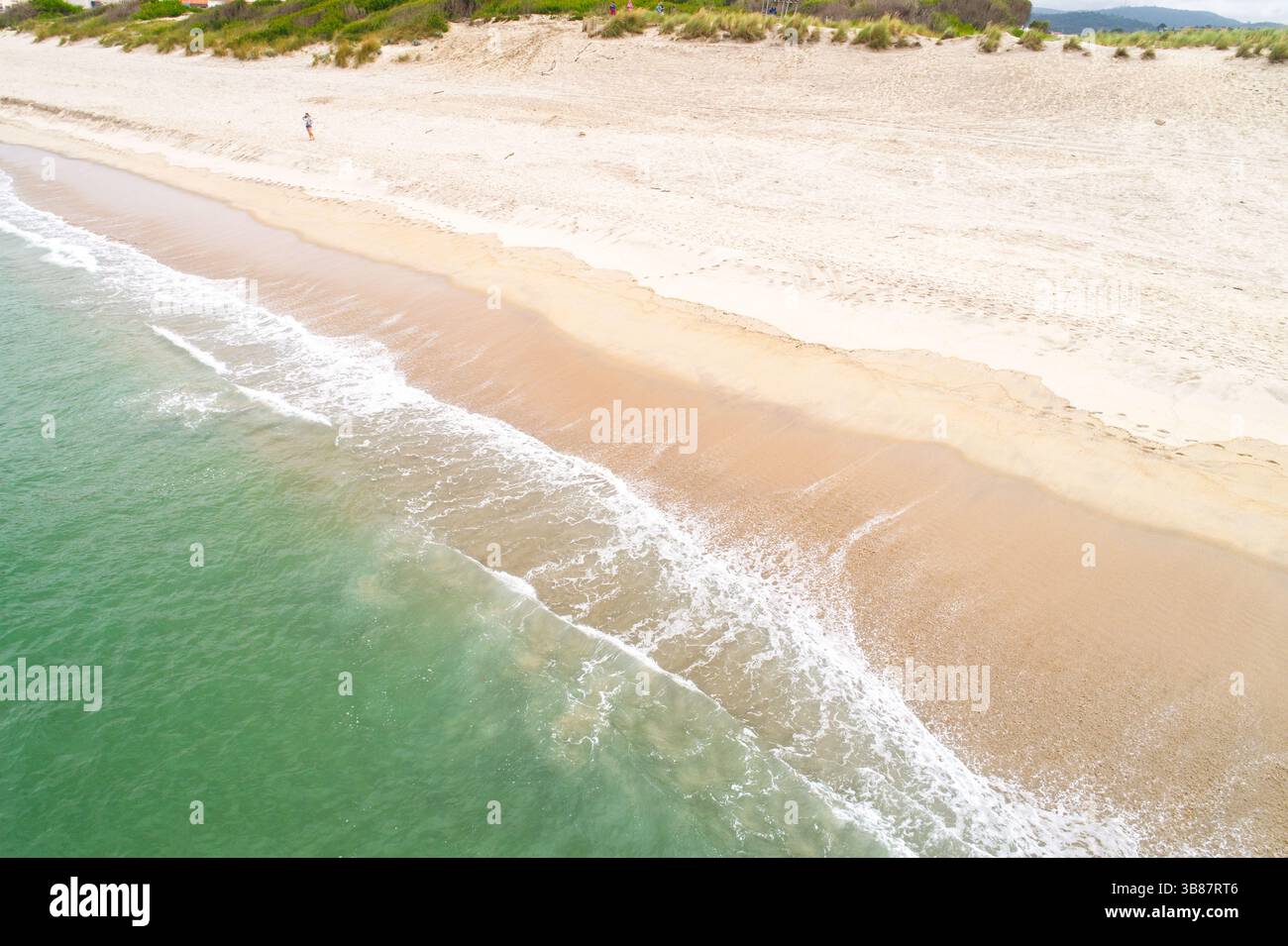 drone aerial shot of a person walking in beach shoreline with sand and ...