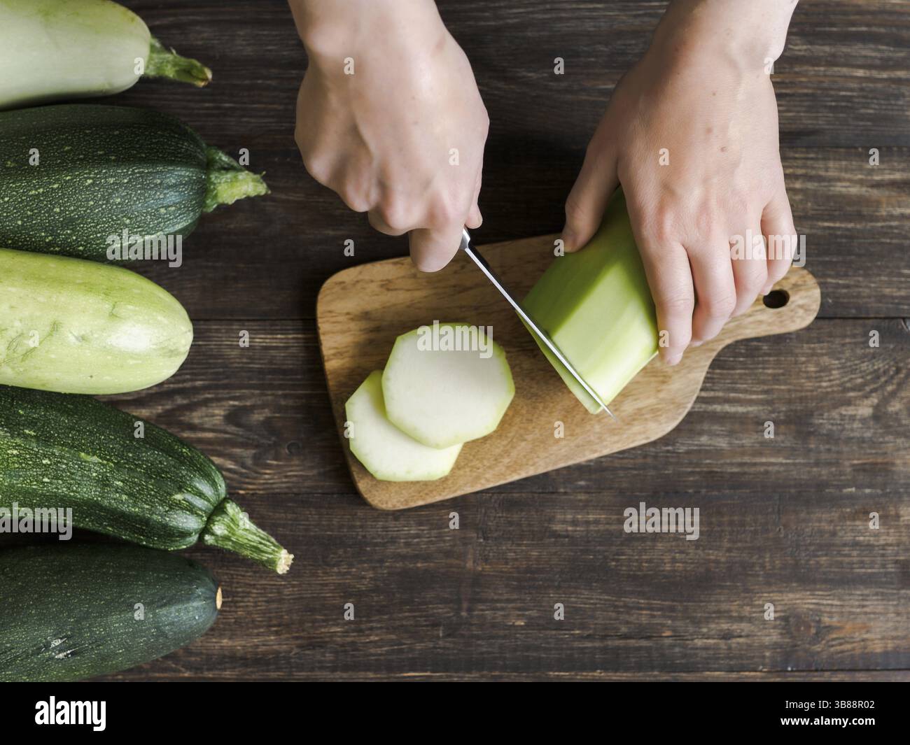 Zucchini harvest. Woman slices zucchini on wooden table. Farm organic ...