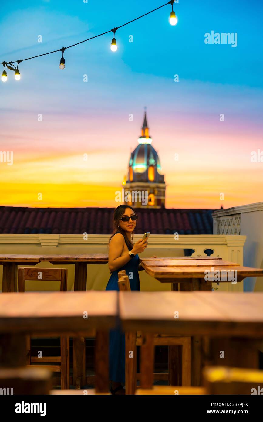 Cheerful young Latina woman in blue dress enjoying colorful sunset at a ...