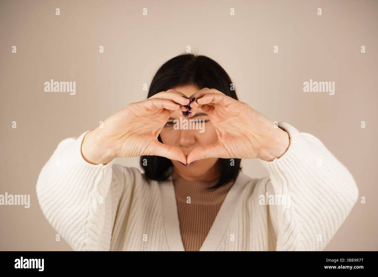 Smiling gently, the woman makes a heart gesture with her hands ...
