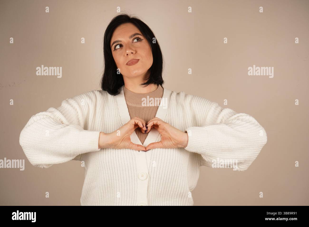 Smiling gently, the woman makes a heart gesture with her hands ...