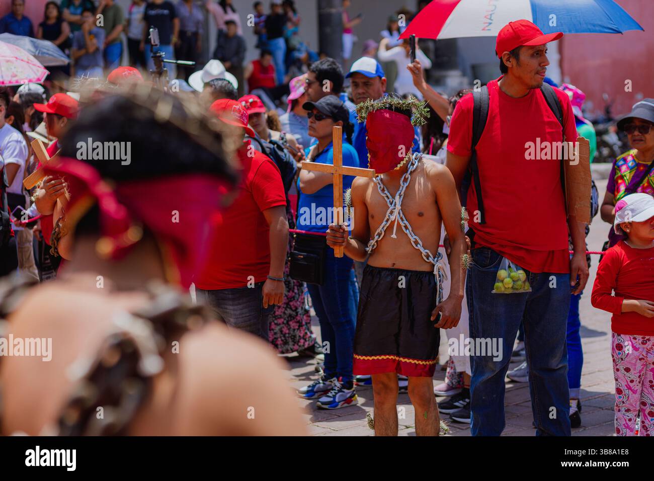 Man with covered face carries a wooden cross, wearing a crown of thorns and chains on his body ...