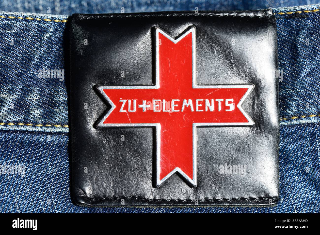 Zu+ Elements jeans label featuring a distinctive red metal cross on ...