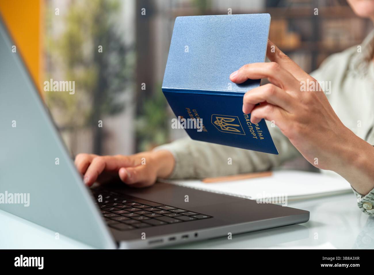 Close up female hands with Ukraine passport entering data using laptop . Ukraininan biometric ...