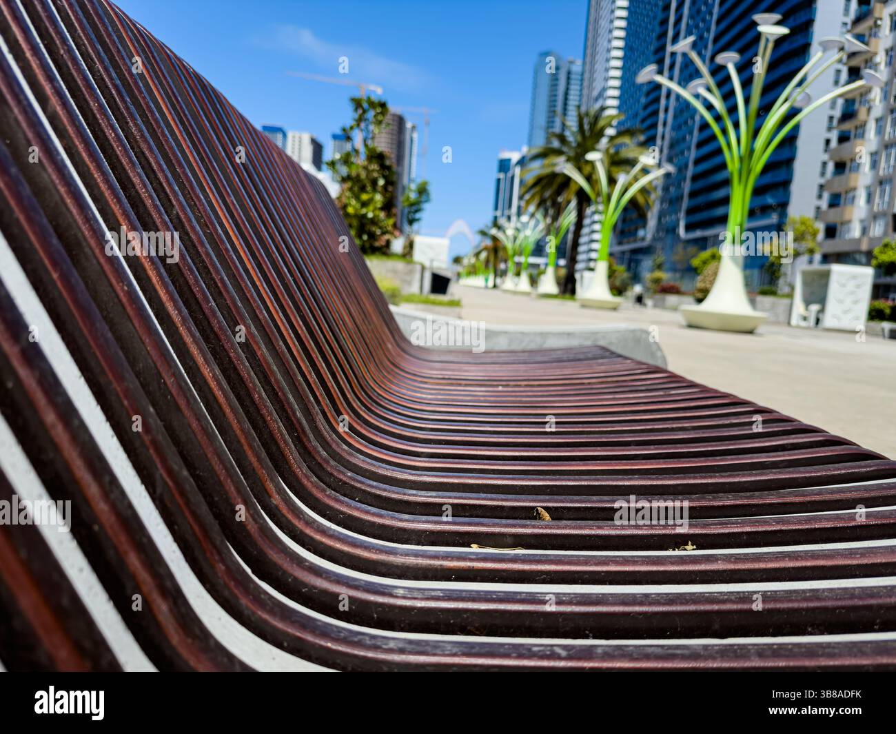 Close-up of curved urban bench with palm trees and modern buildings in ...
