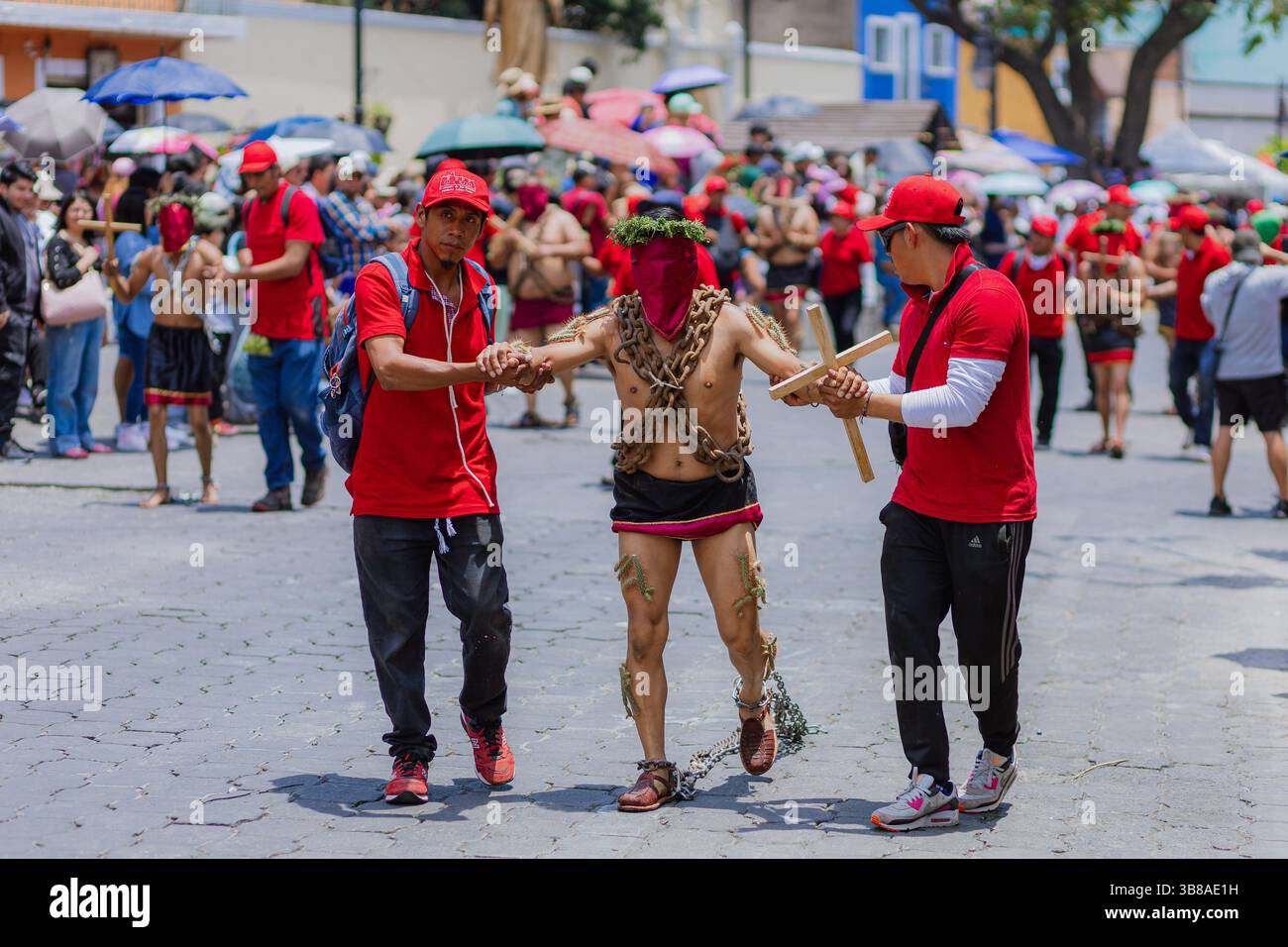 Man with covered face carries a wooden cross, wearing a crown of thorns and chains on his body ...