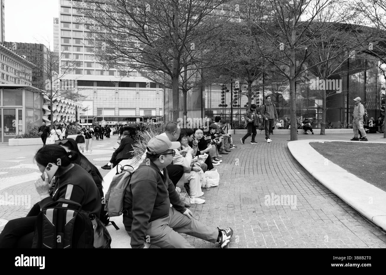 People resting and eating on curved benches in a busy public square ...