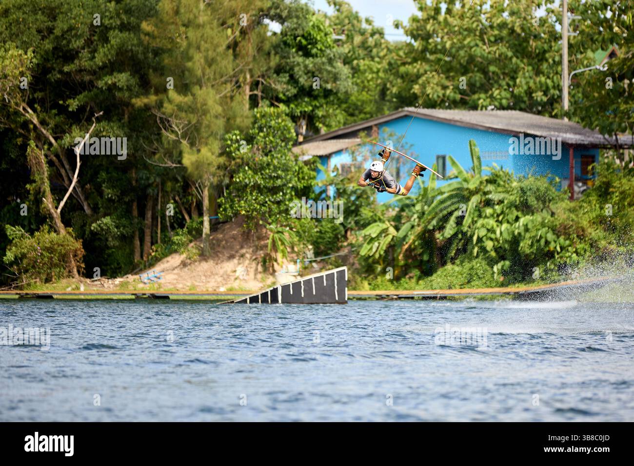 Skilled wakeboarder in mid-air performing a trick over an obstacle ...