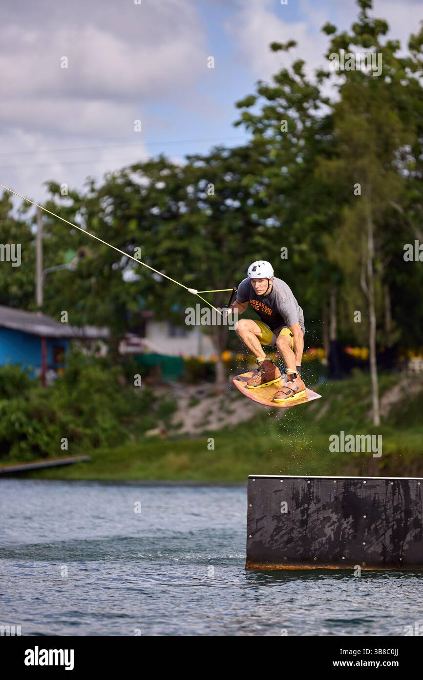 Skilled wakeboarder in mid-air performing a trick over an obstacle ...