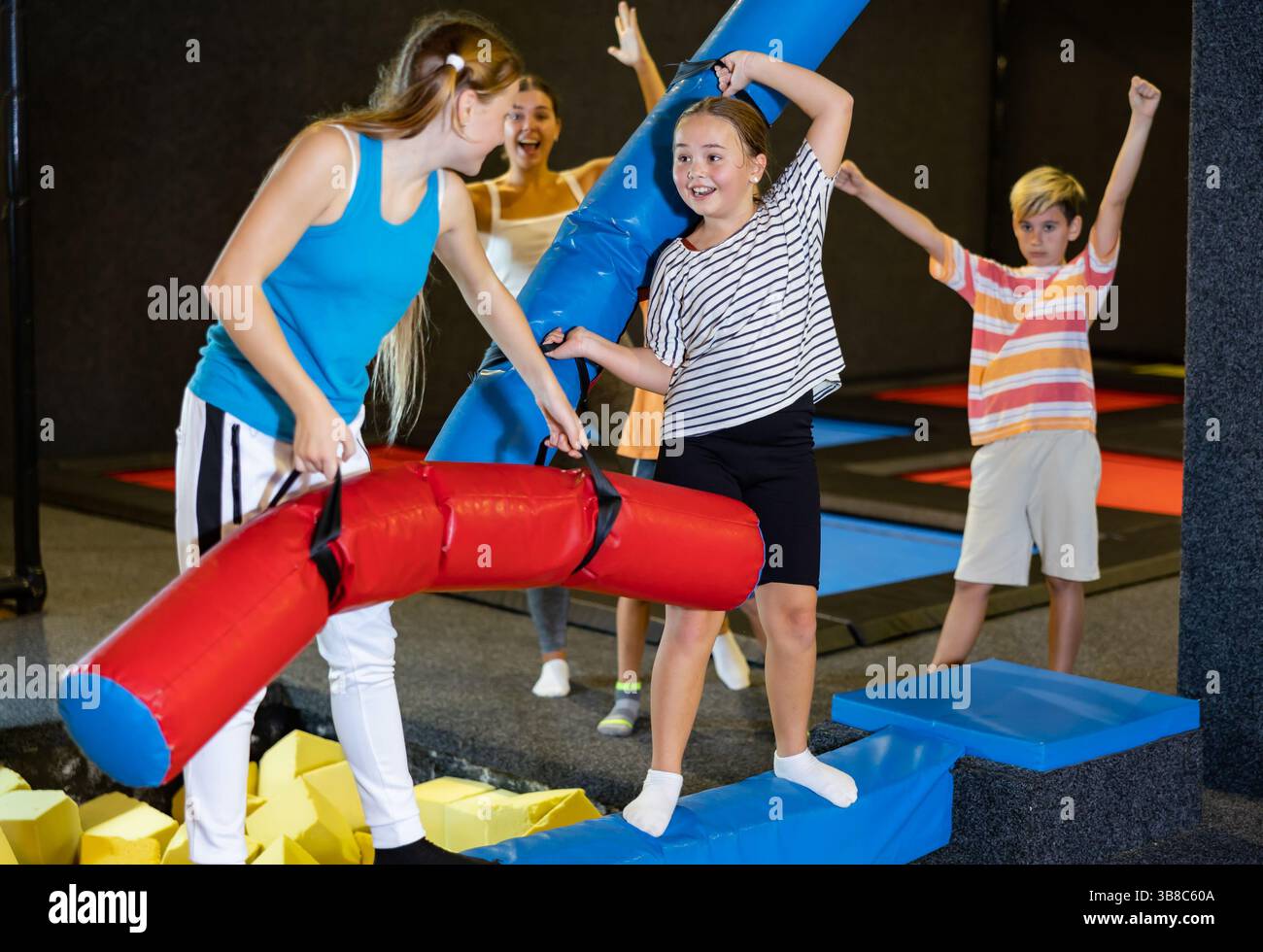 Tween girl fighting by pugil stick with female friend on inflatable ...
