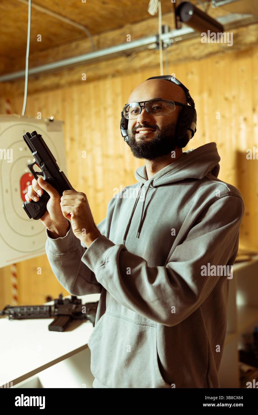 Portrait of happy Arab man in shooting range cocking handgun, setting ...