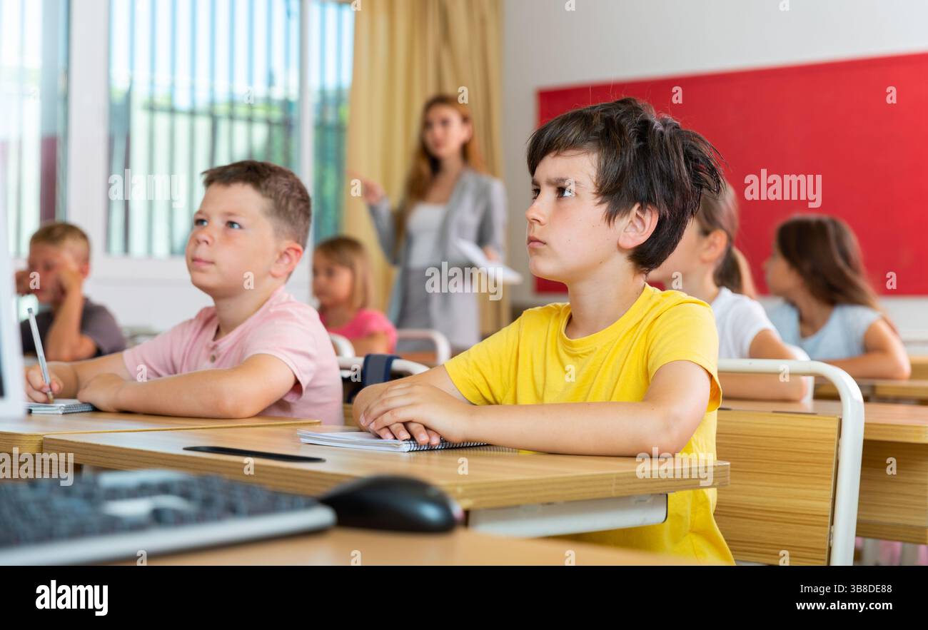 Tween boy listening to schoolteacher and writing in notebook in class ...