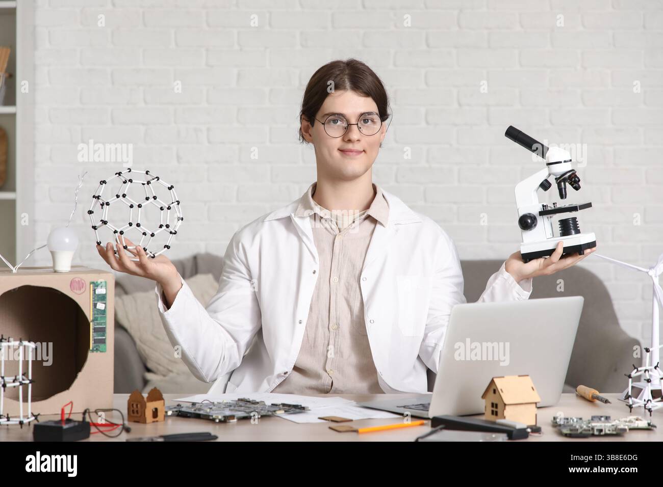 Male inventor with molecular model and microscope at table in office ...