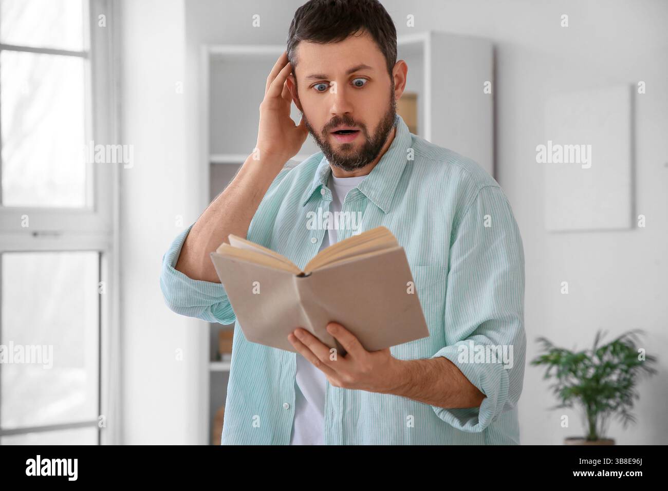 Shocked young man reading book at home Stock Photo - Alamy