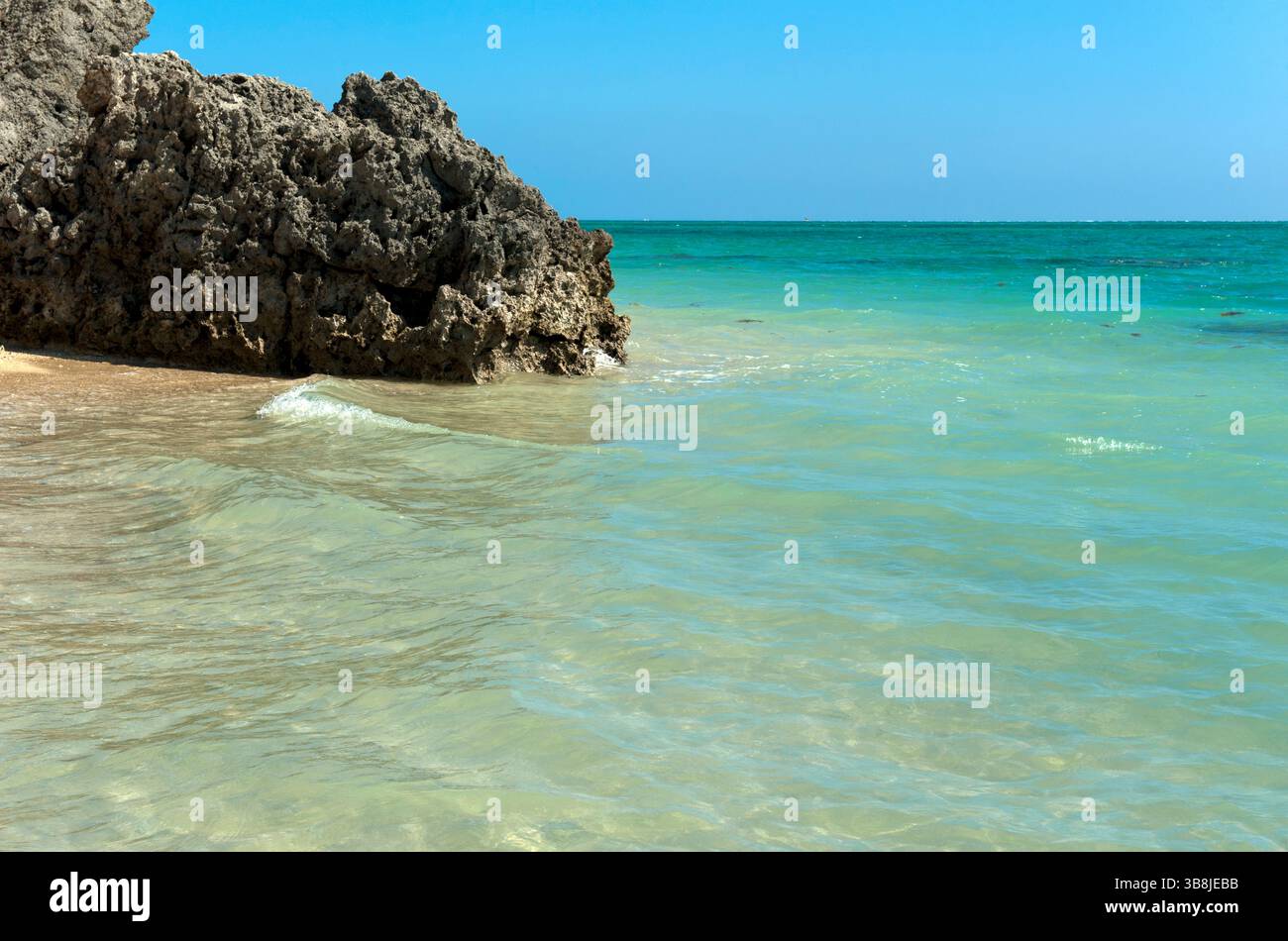 Volcanic rock outcropping sits close to the shore in the azure seas of ...
