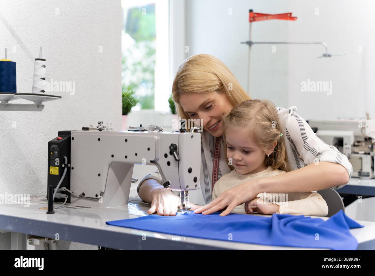 Mom and daughter sitting together at the sewing machine and looking ...