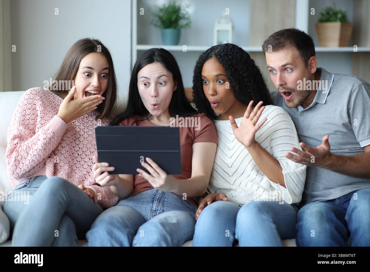 Surprised group of friends checking tablet content sitting on a couch ...
