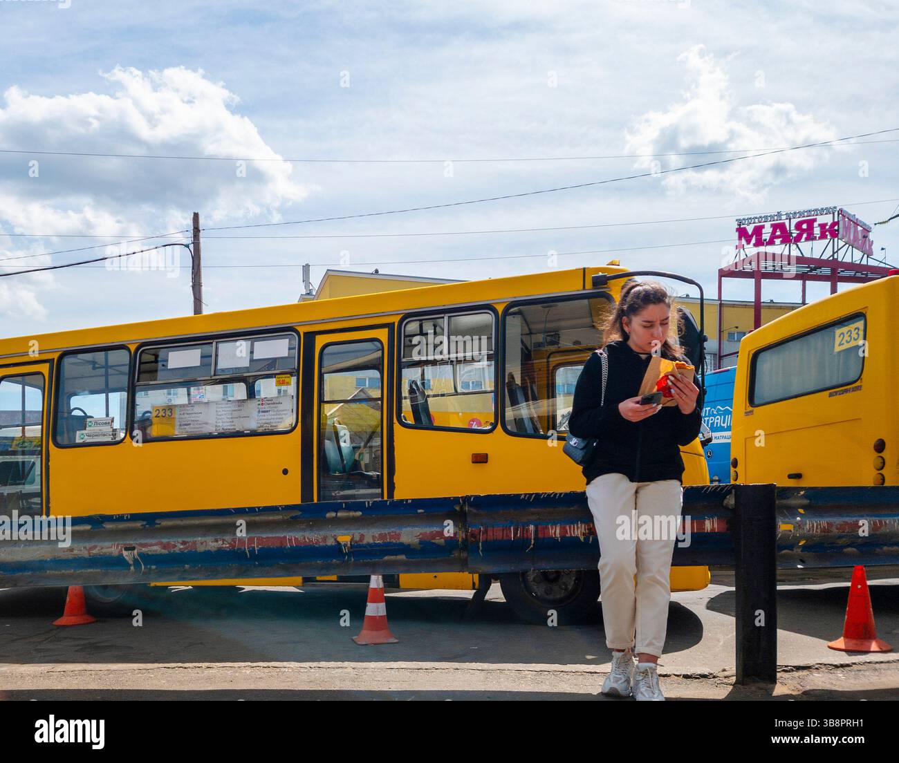 Kyiv, Ukraine - 1st May, 2025. A woman enjoys street food while seated on a barrier, surrounded ...