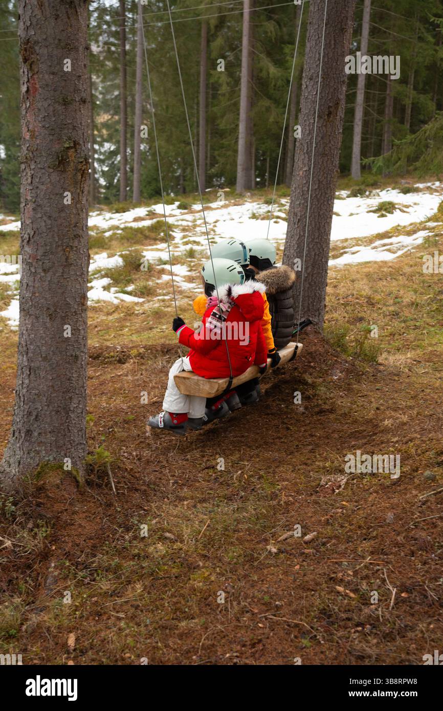 Siblings clad in bright winter coats swing together, laughing heartily as they embrace the crisp ...