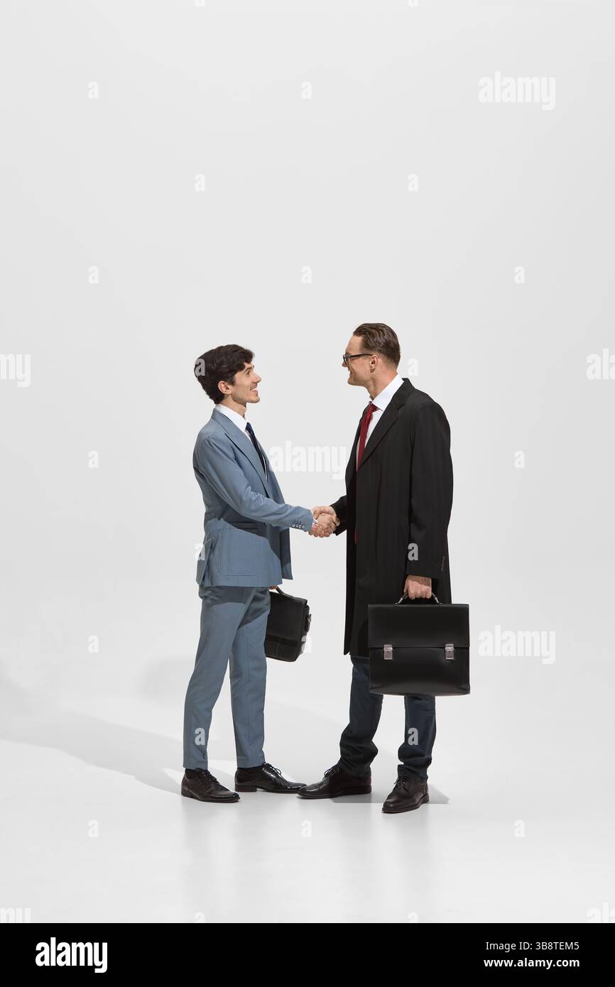 Two formally dressed men engage in handshake against white studio ...