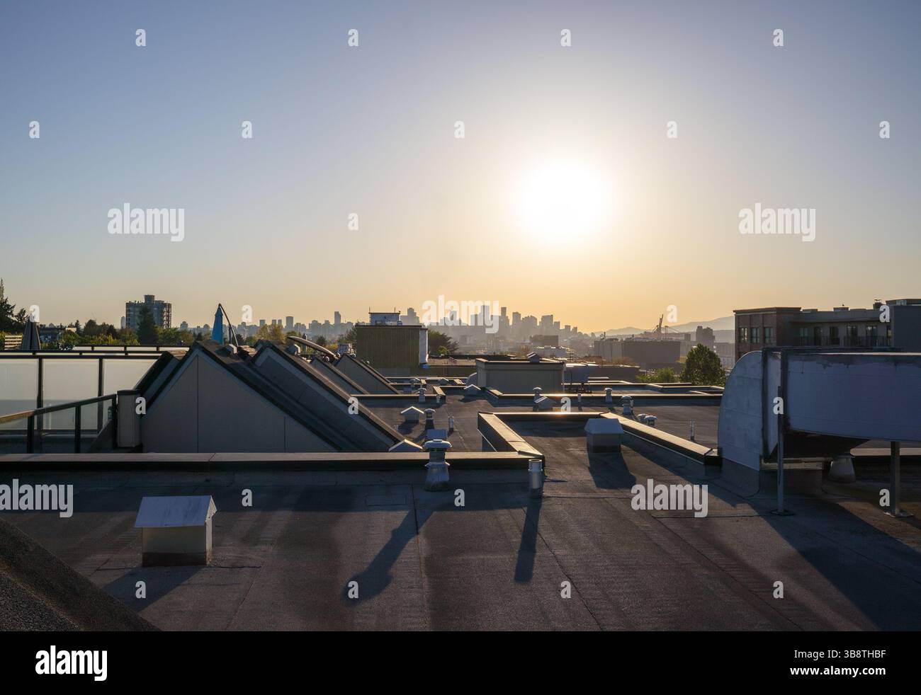 Flat roof with city skyline during sunset. Backlit view of downtown Vancouver far back. 2-ply ...