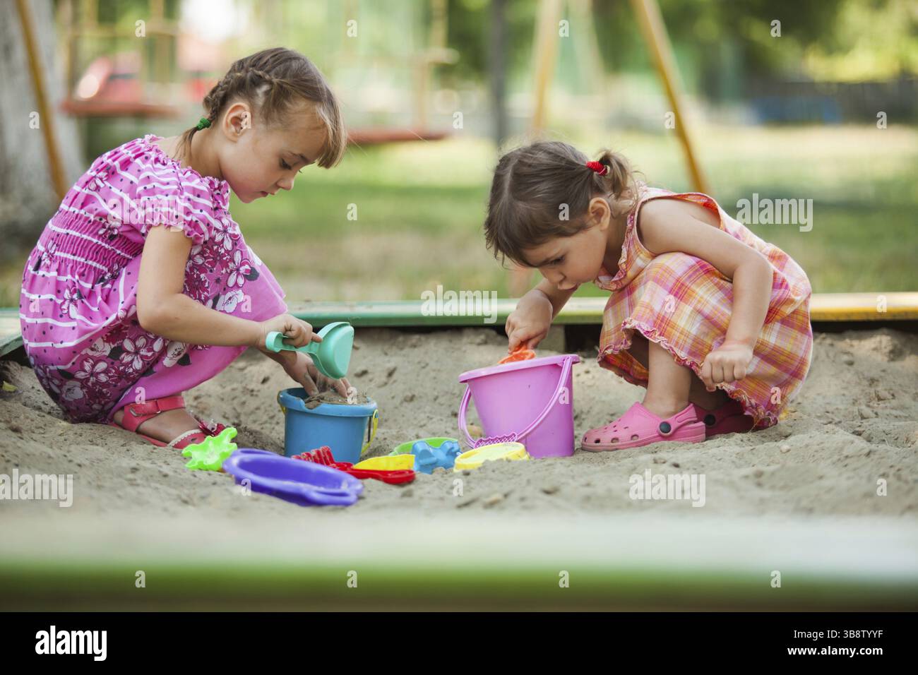 Two girls play in the sandbox at the playground Stock Photo - Alamy