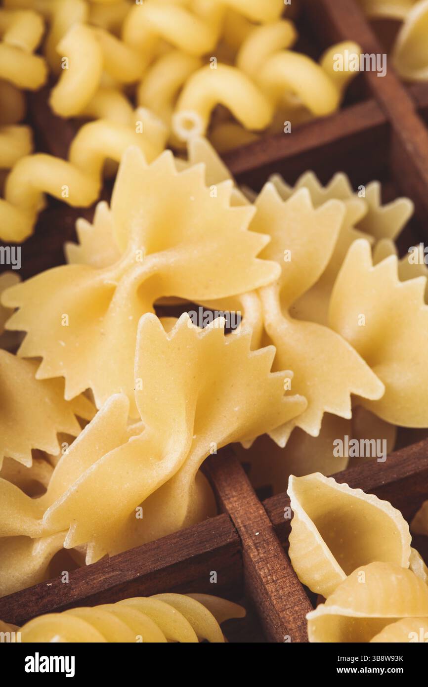 Various pasta types in the wooden box on the table. Close up farfalle ...