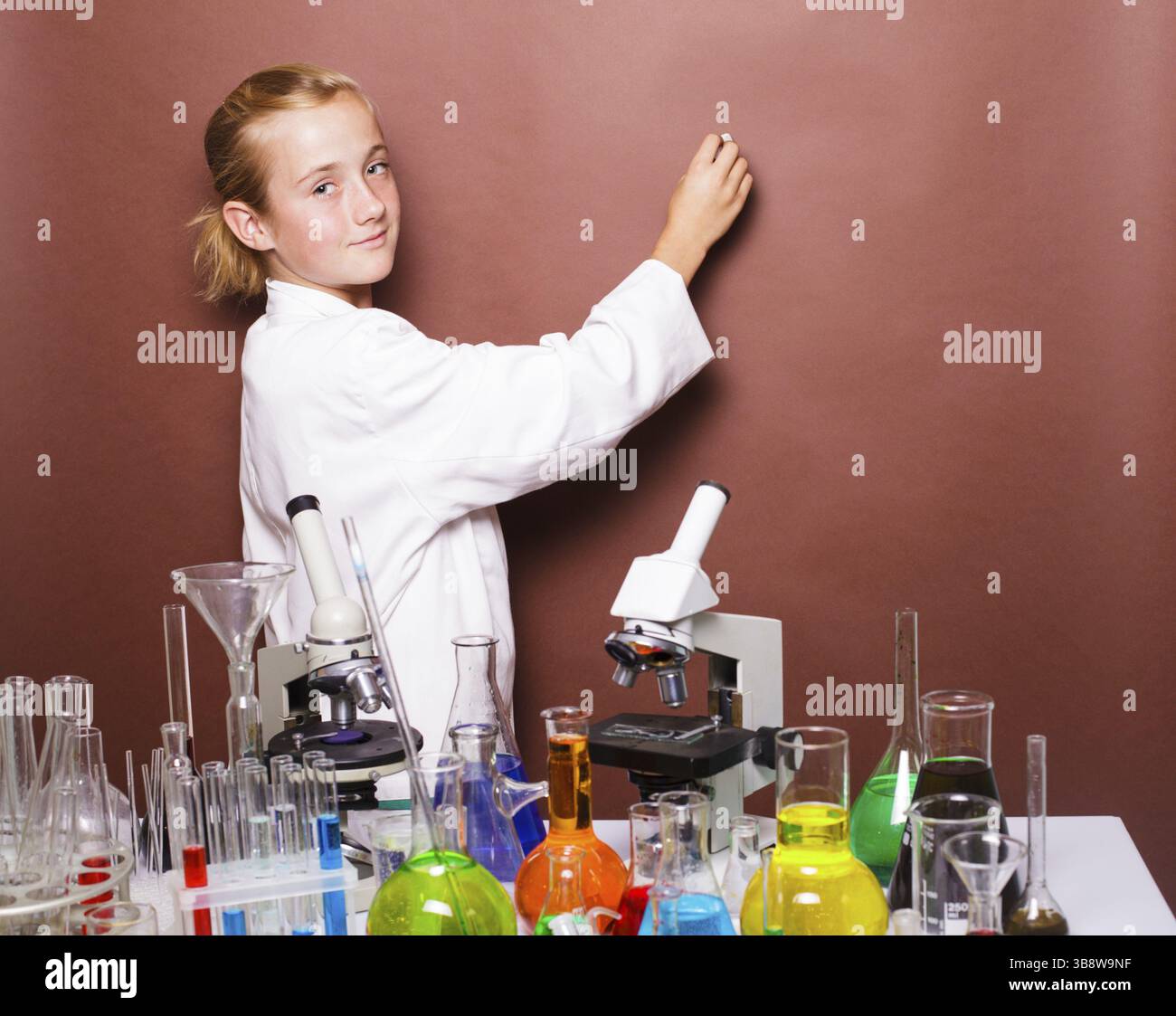 Schoolgirl with chalk standing near blackboard in the laboratory ...