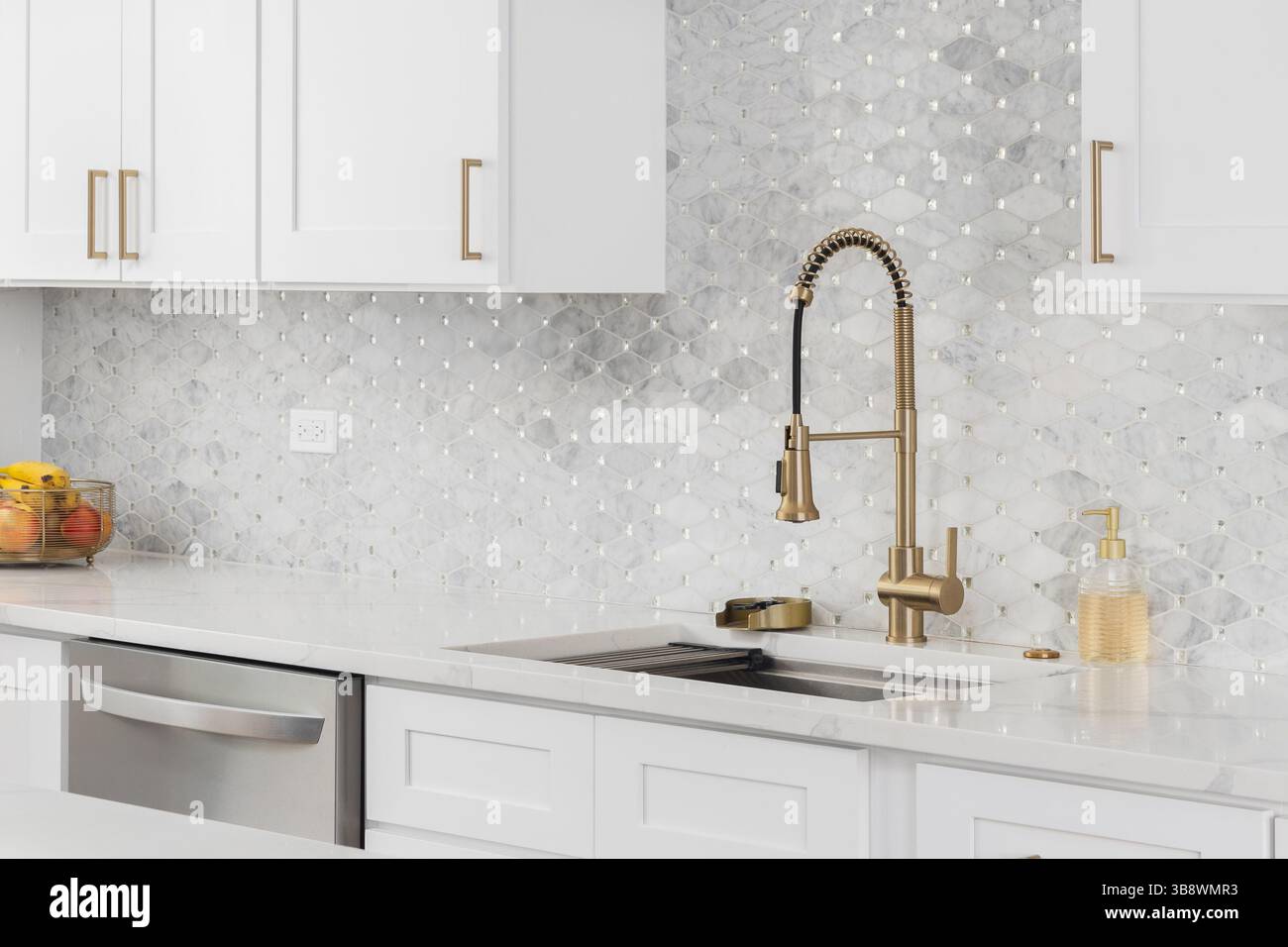 A kitchen with a gold faucet, white marble mosaic tile backsplash ...
