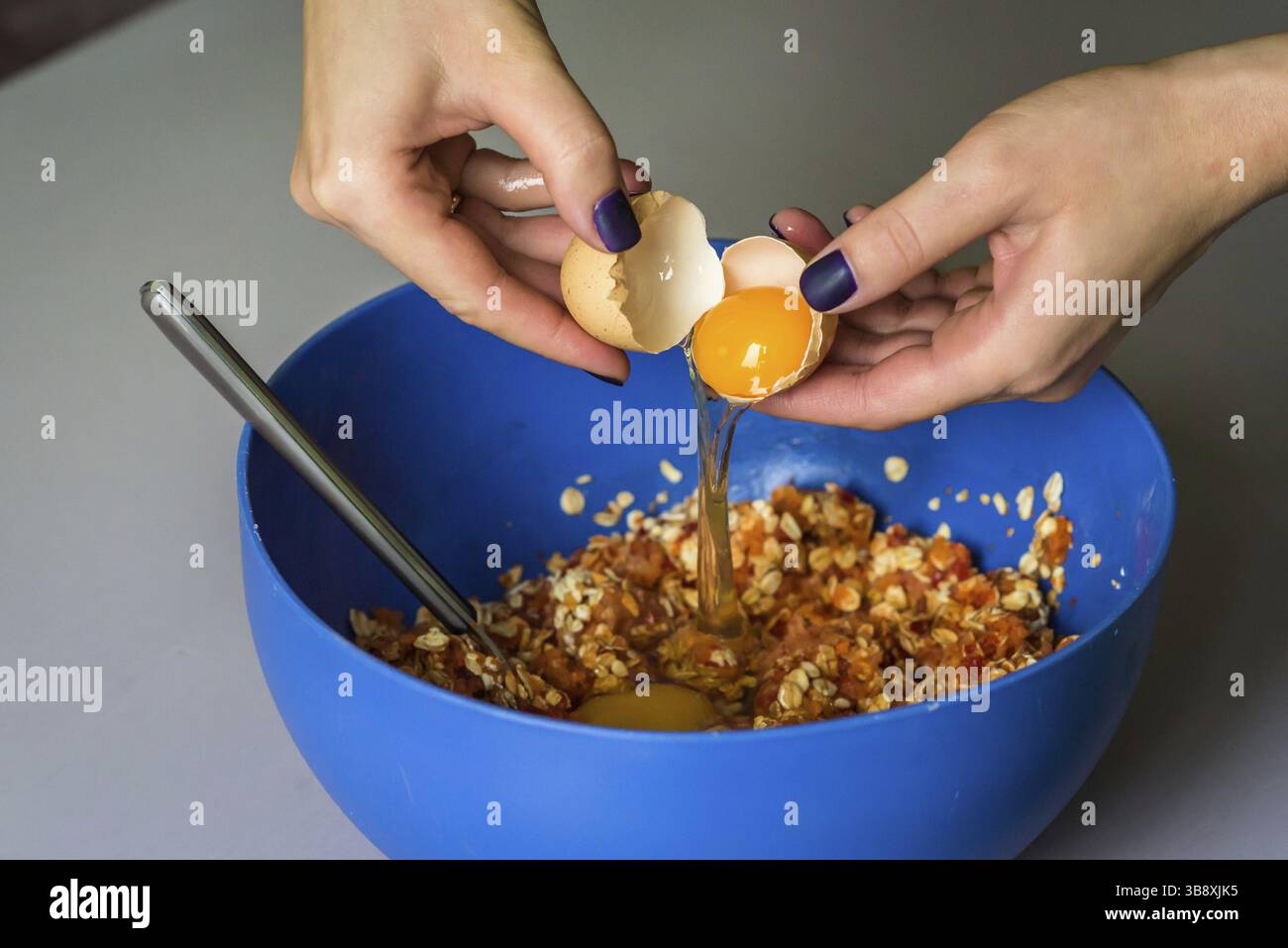 Hand pours out raw egg of the shell in blue bowl Stock Photo - Alamy
