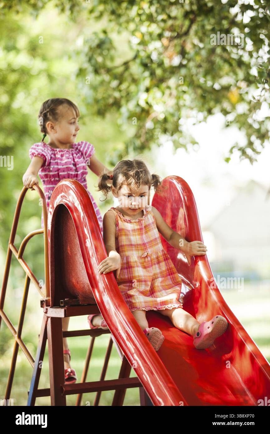 Two preschool girls on the slide at the playground Stock Photo - Alamy