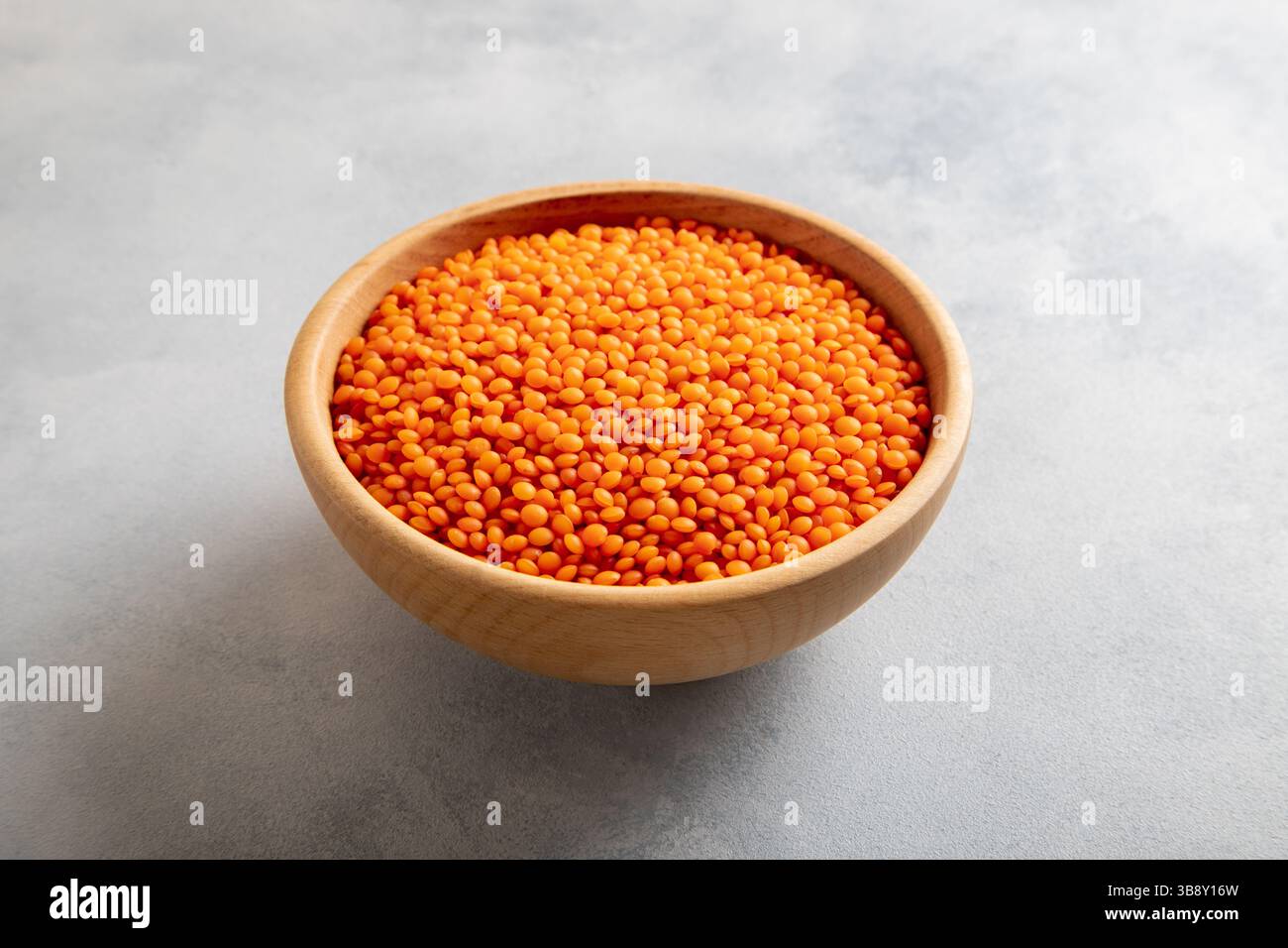 Red lentil grains in a wooden bowl on light blue background. Top view ...
