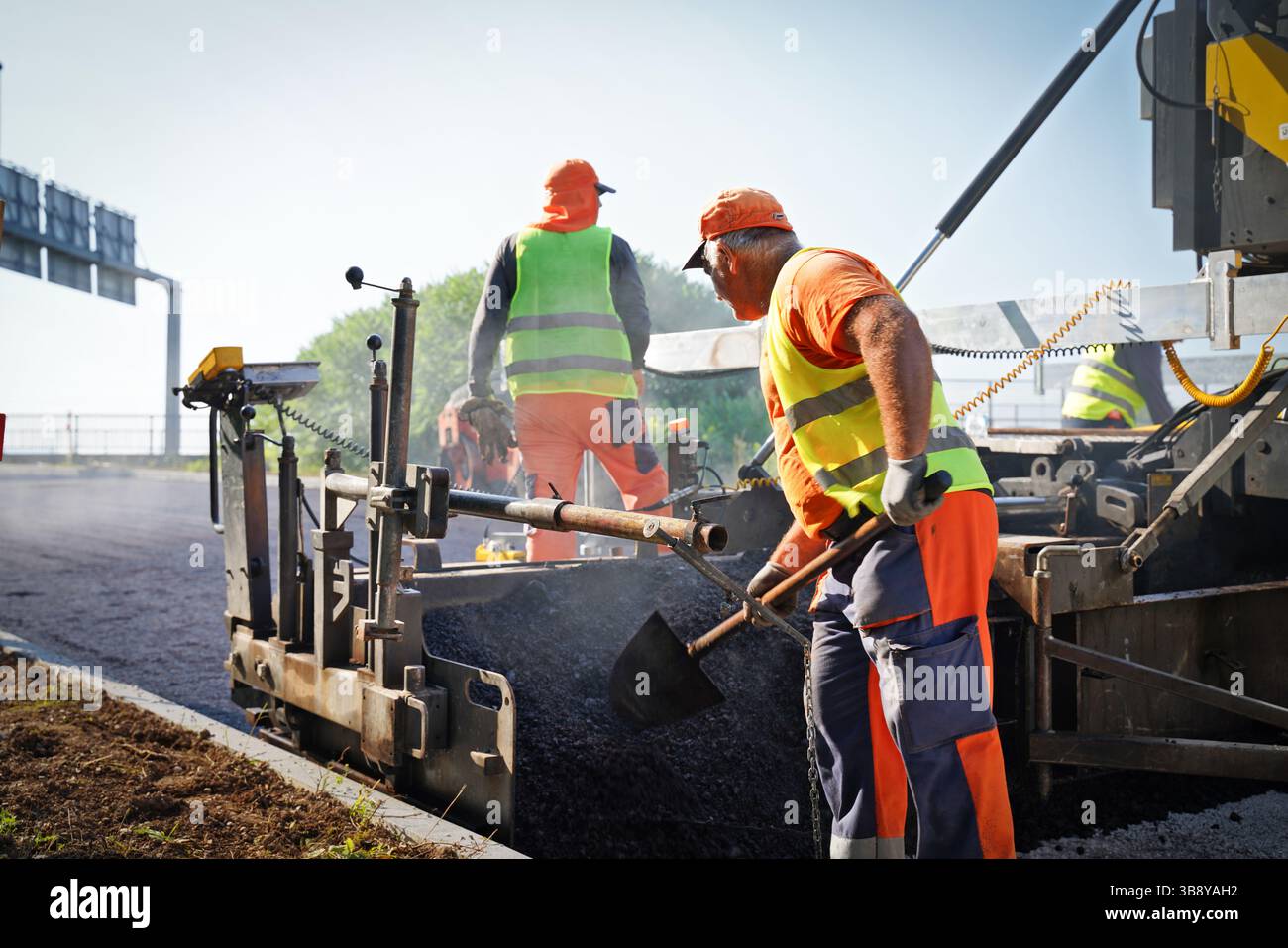 Construction worker using shovel to spread hot fresh asphalt in front ...