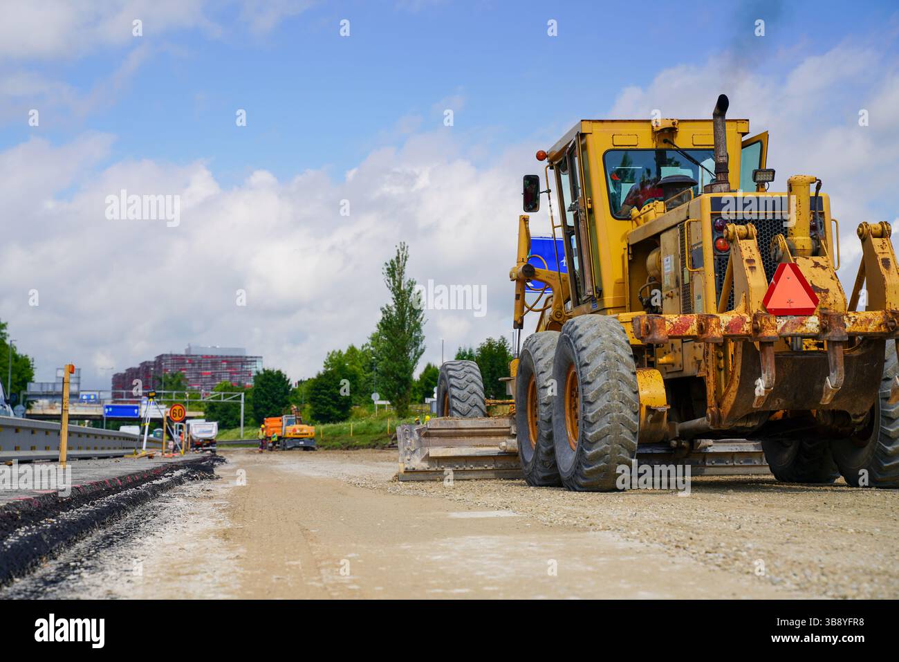Motor grader spreading gravel to create a smooth and level surface foundation for a new asphalt ...