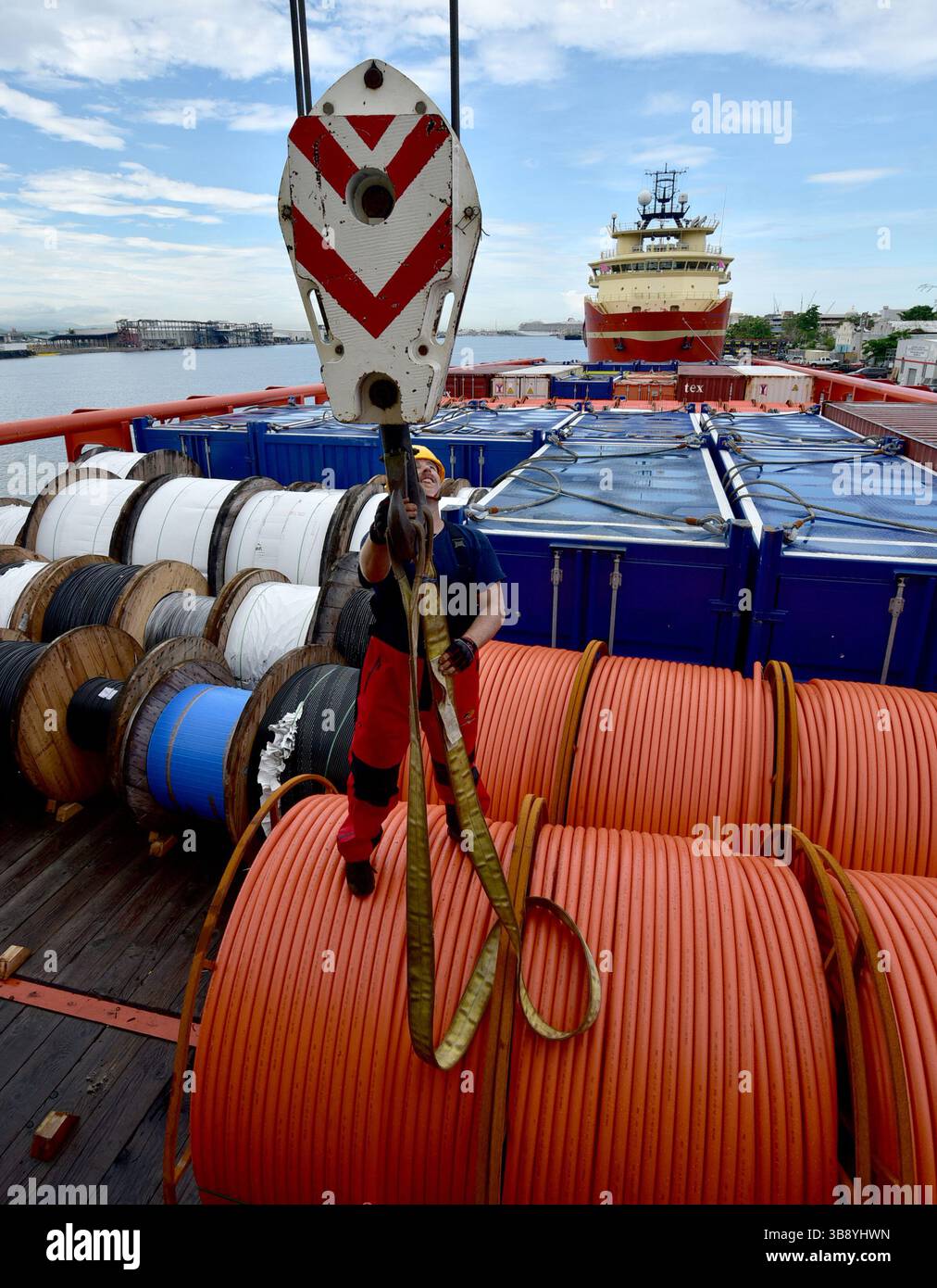Crane unloads rolls of PVC cable sheathing from cargo ship. Worker ...