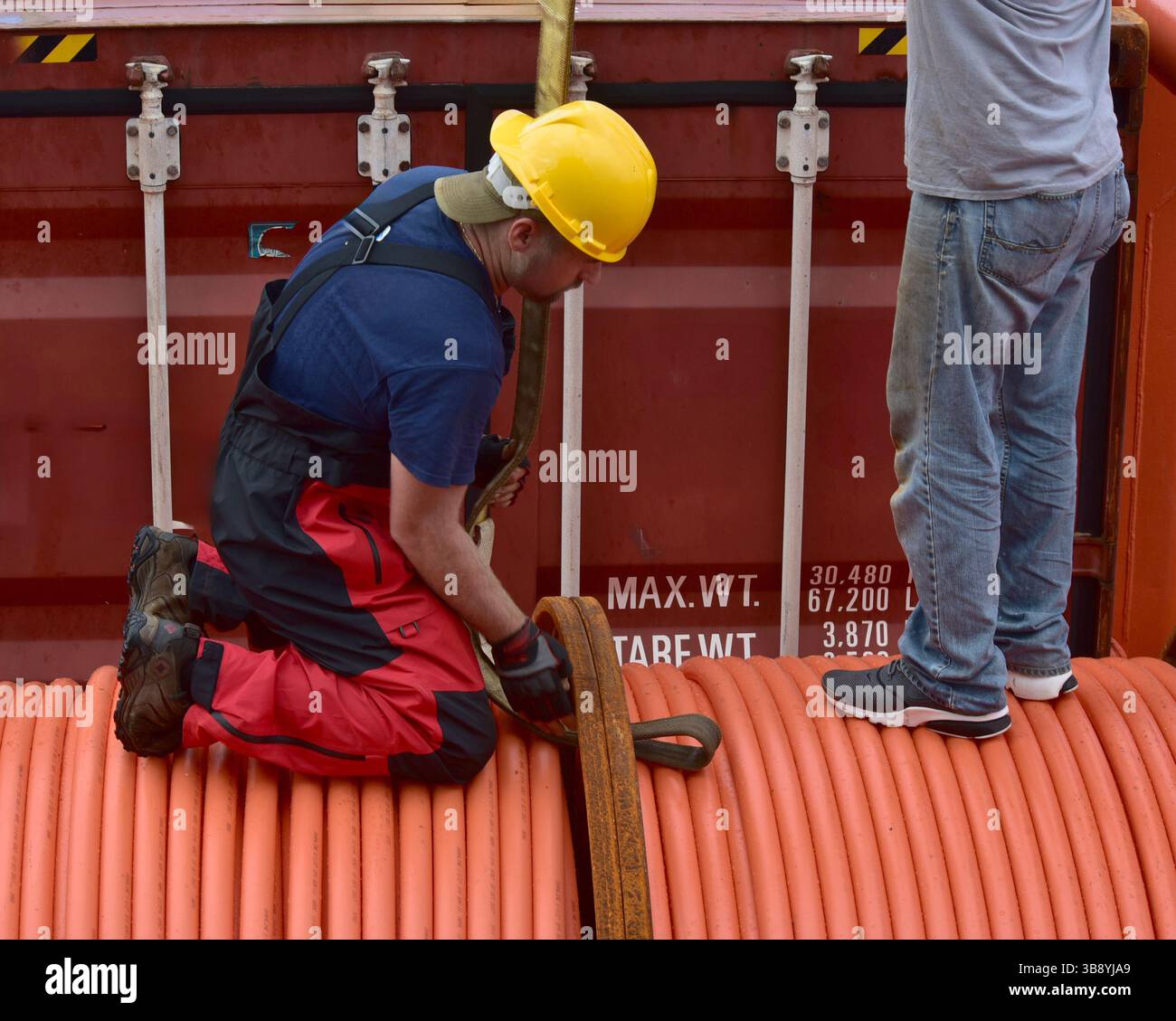 Crane unloads rolls of PVC cable sheathing from cargo ship. Workers ...