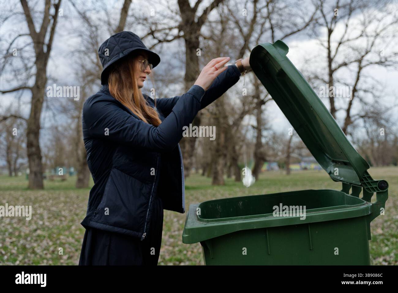 A girl dressed warmly in black hat and jacket disposes of trash ...