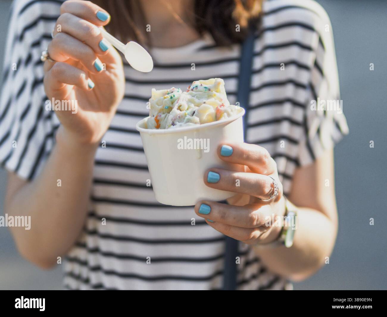 Rolled ice cream in cone cup in woman hands. Woman in striped dress ...