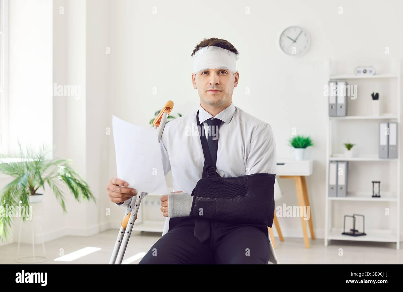 Young injured man with broken arm and bandaged head working in office ...