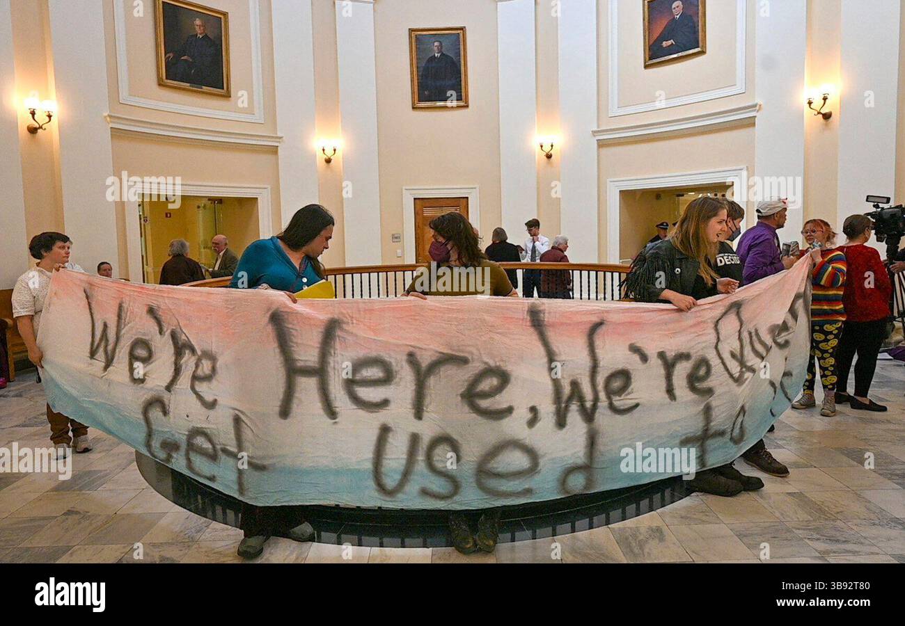People hold a banner reading, "We're Here, We're Queer Get Used To It!" in fourth floor rotunda ...