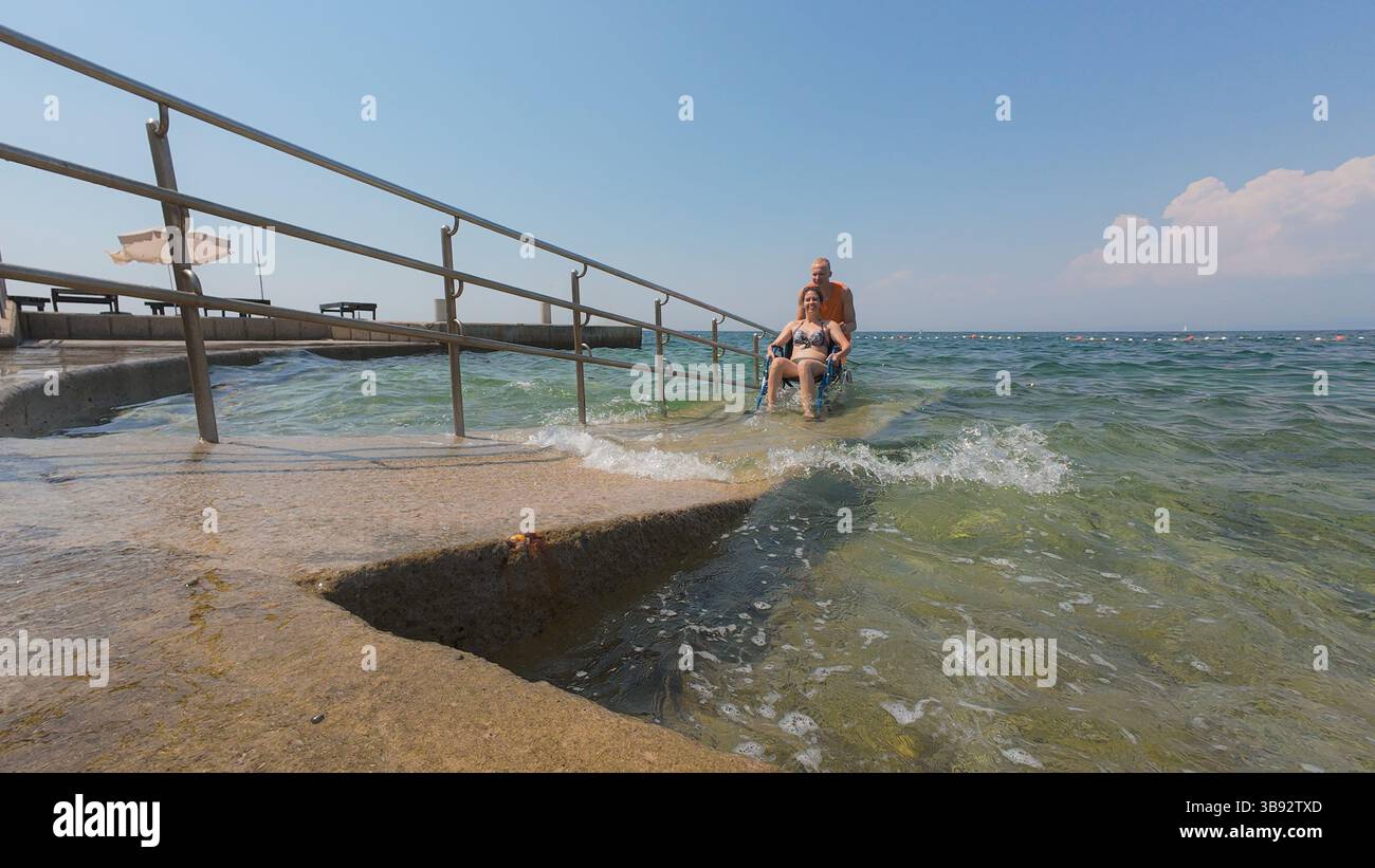 Relaxed woman with disability, exiting the sea water with the help of ...
