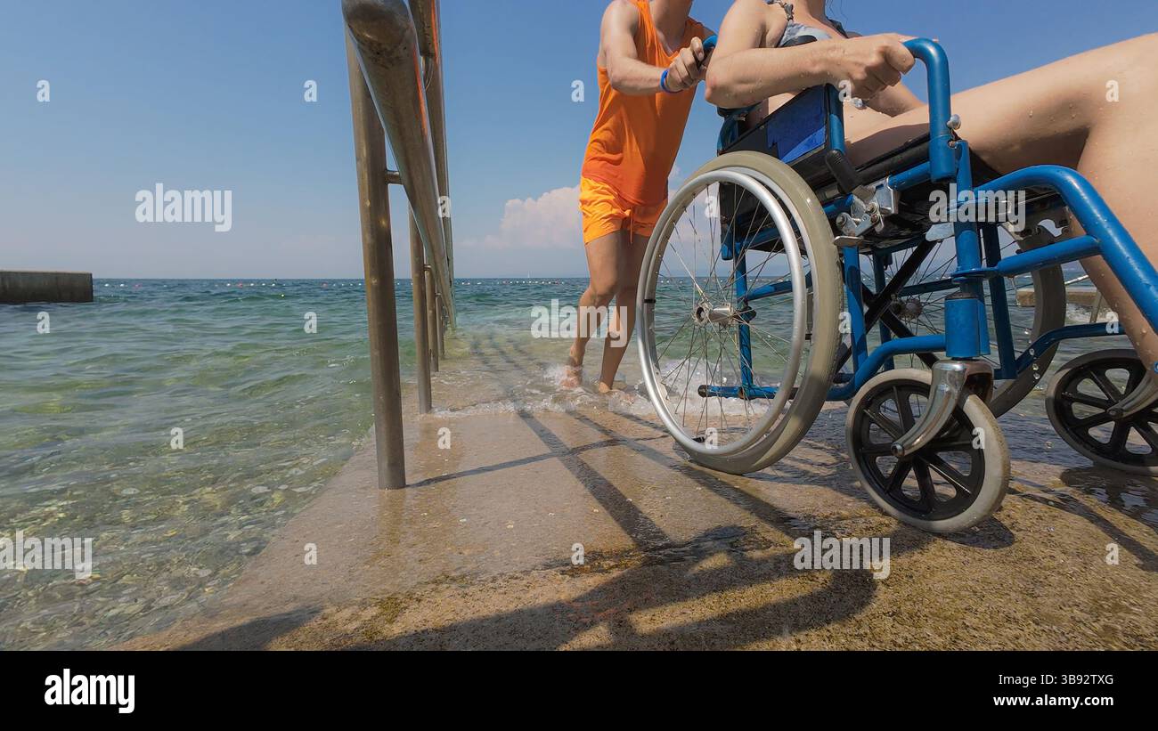 Lifeguard helping a woman with disability enter the water across the ...