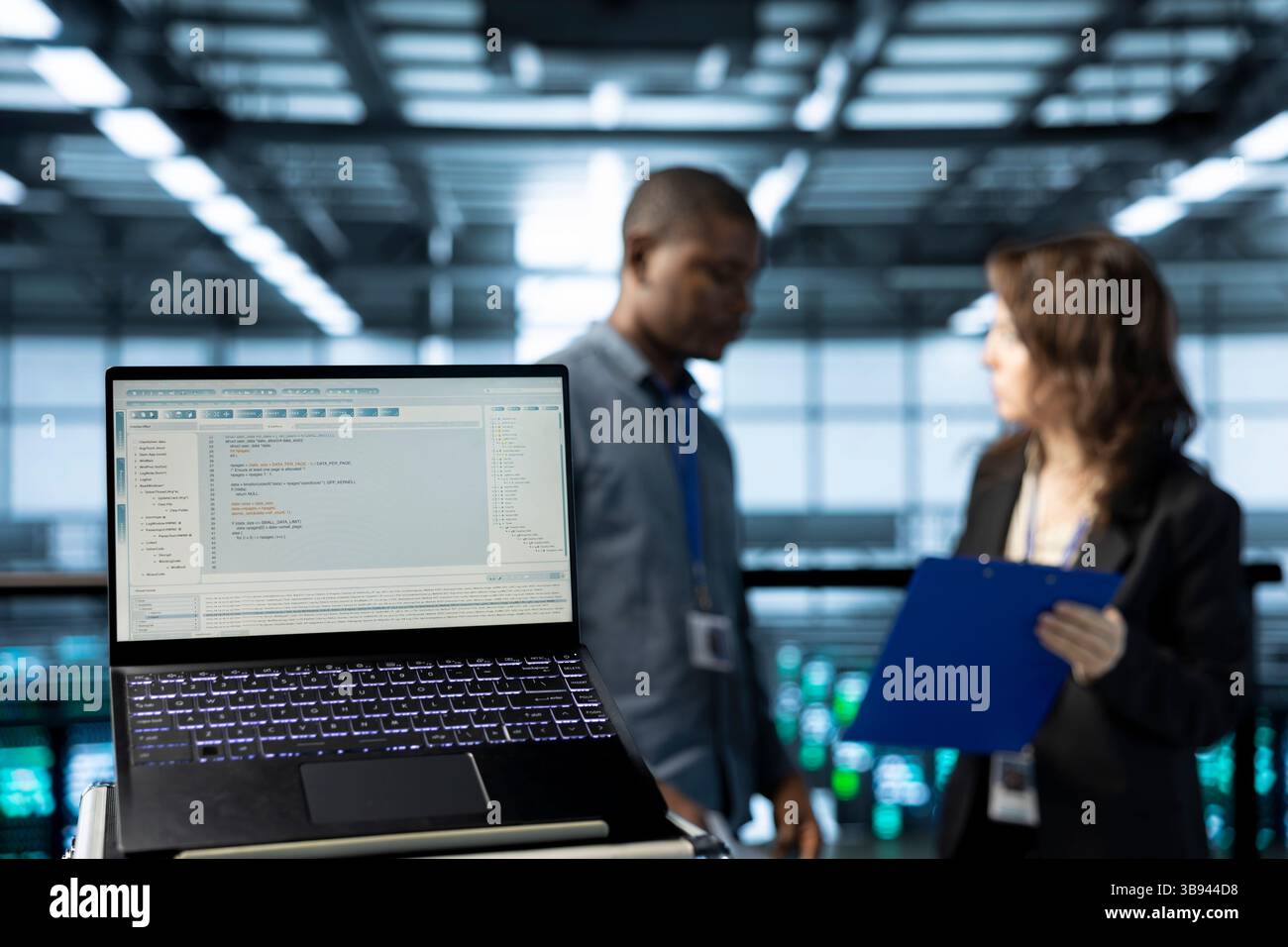 Close up of code lines on laptop screen in front of data center engineers checking documents ...
