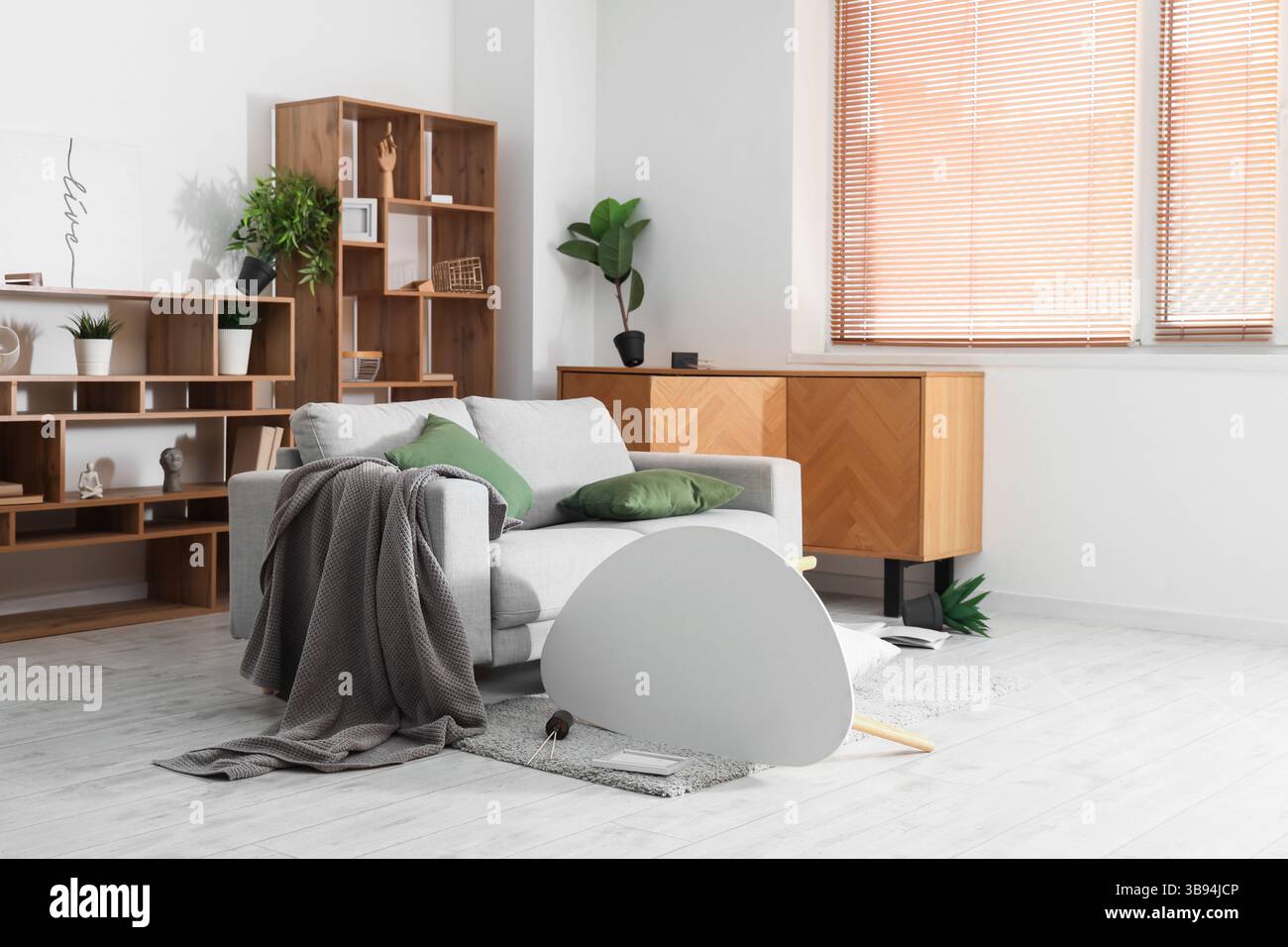 Interior of messy room with grey sofa and overturned furniture after ...