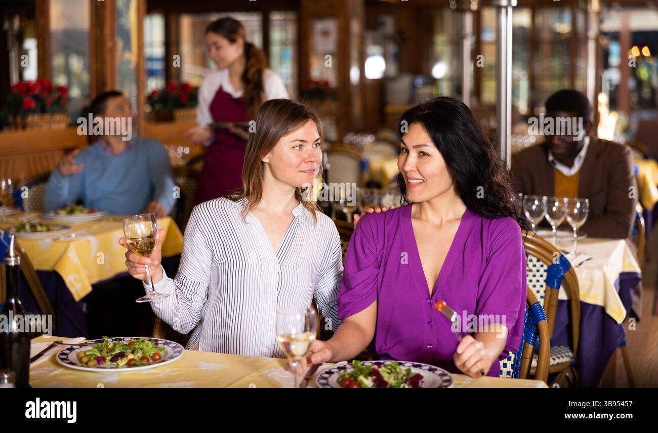 Cheerful Asian woman with female friend having dinner in restaurant ...