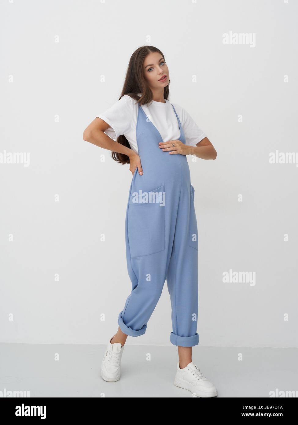 A confident woman poses gracefully in bright blue overalls and a casual ...
